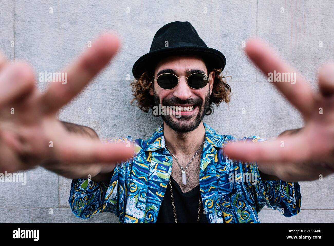 Happy man wearing Hawaiian shirt showing peace sign in front of wall ...