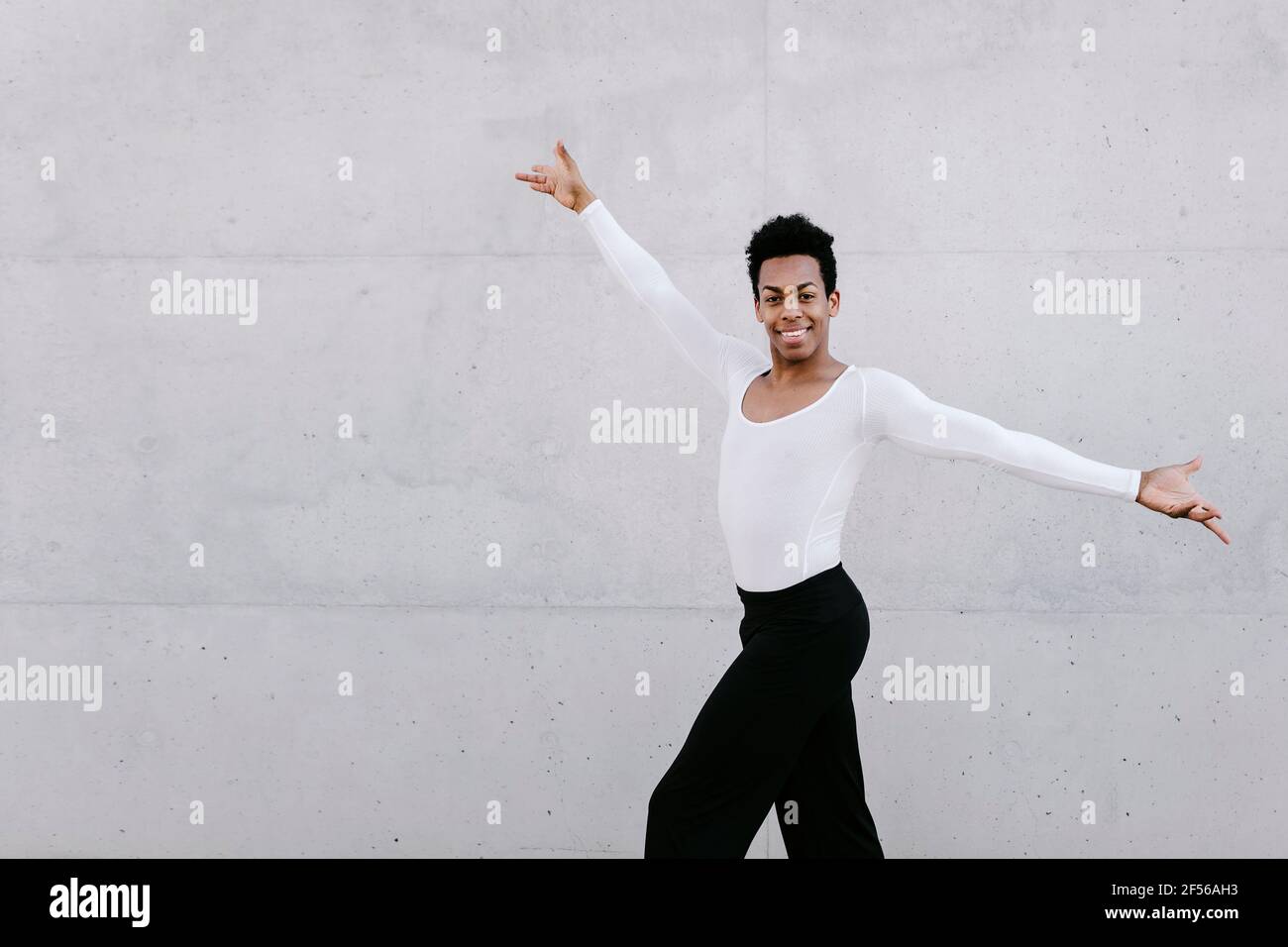 Smiling male urban dancer practicing by stretching arms against white ...