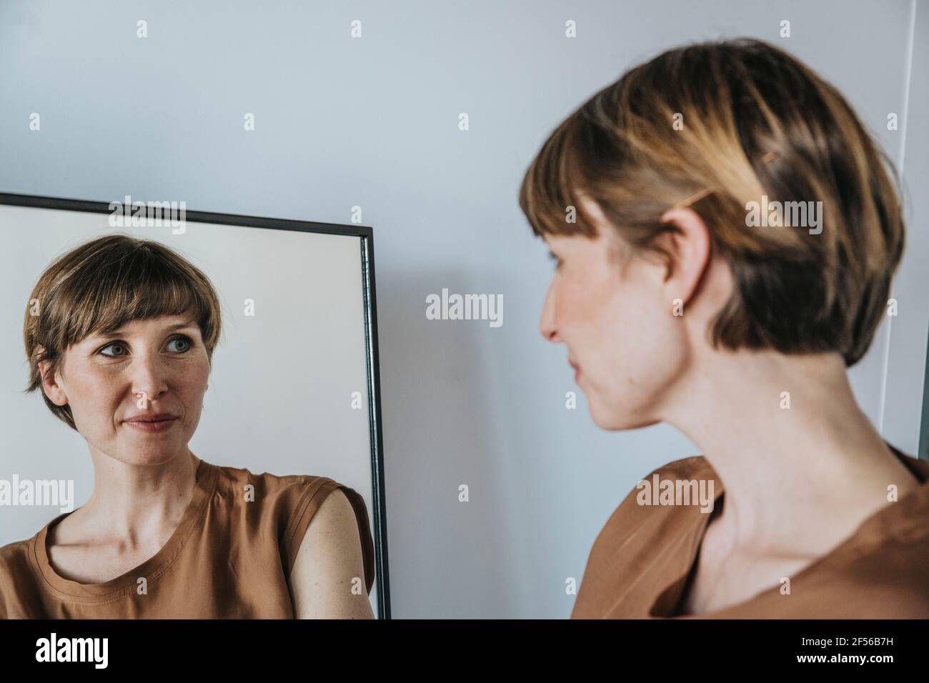 Thoughtful woman looking at reflection in mirror Stock Photo - Alamy