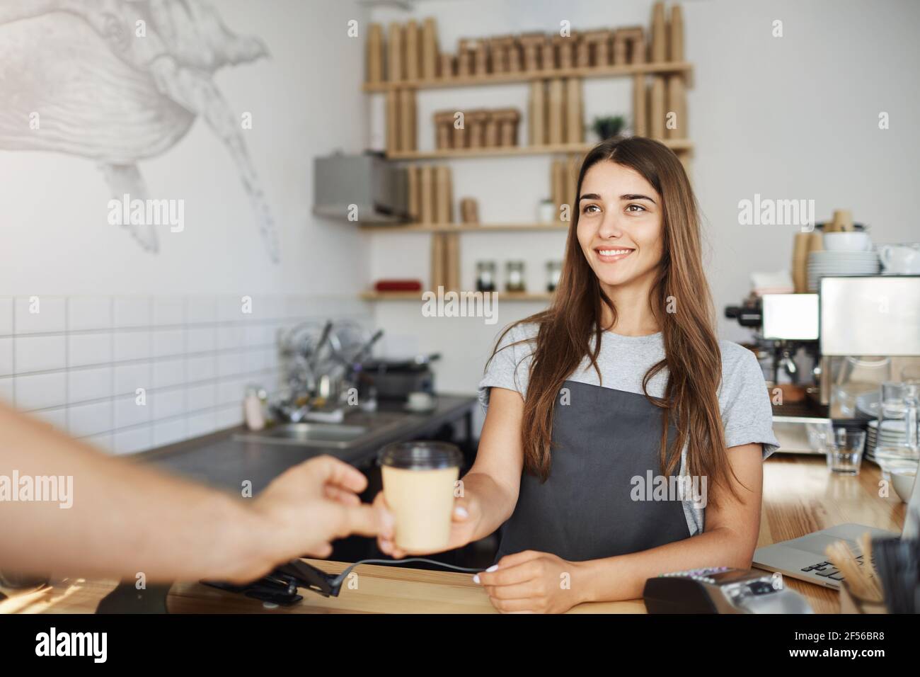 Young lady barista serving coffee to go to her first customer today ...