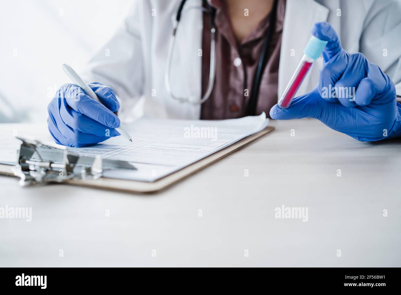 Female doctor holding blood sample while writing medical report at desk ...