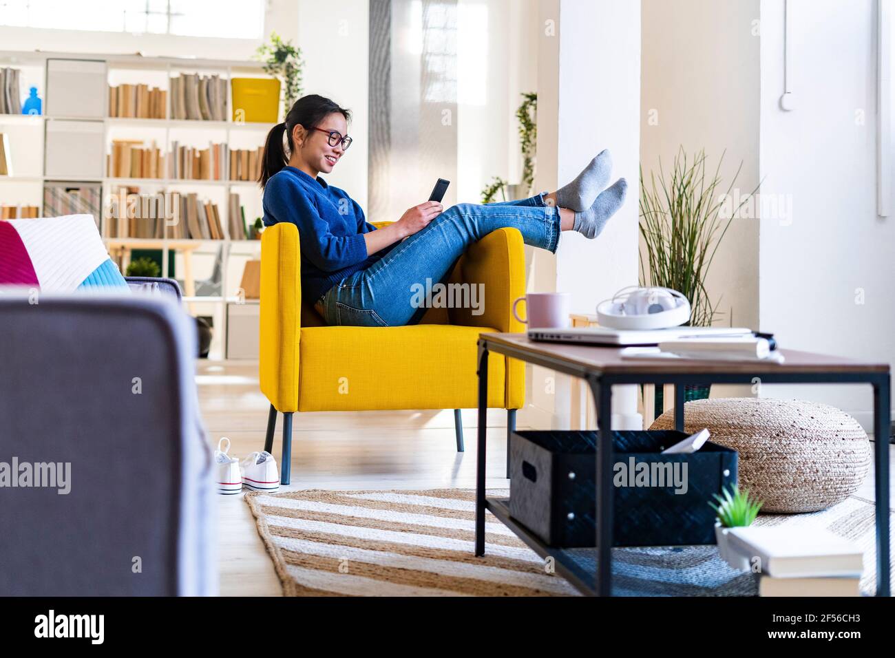 Woman using mobile phone while sitting on chair at home Stock Photo - Alamy