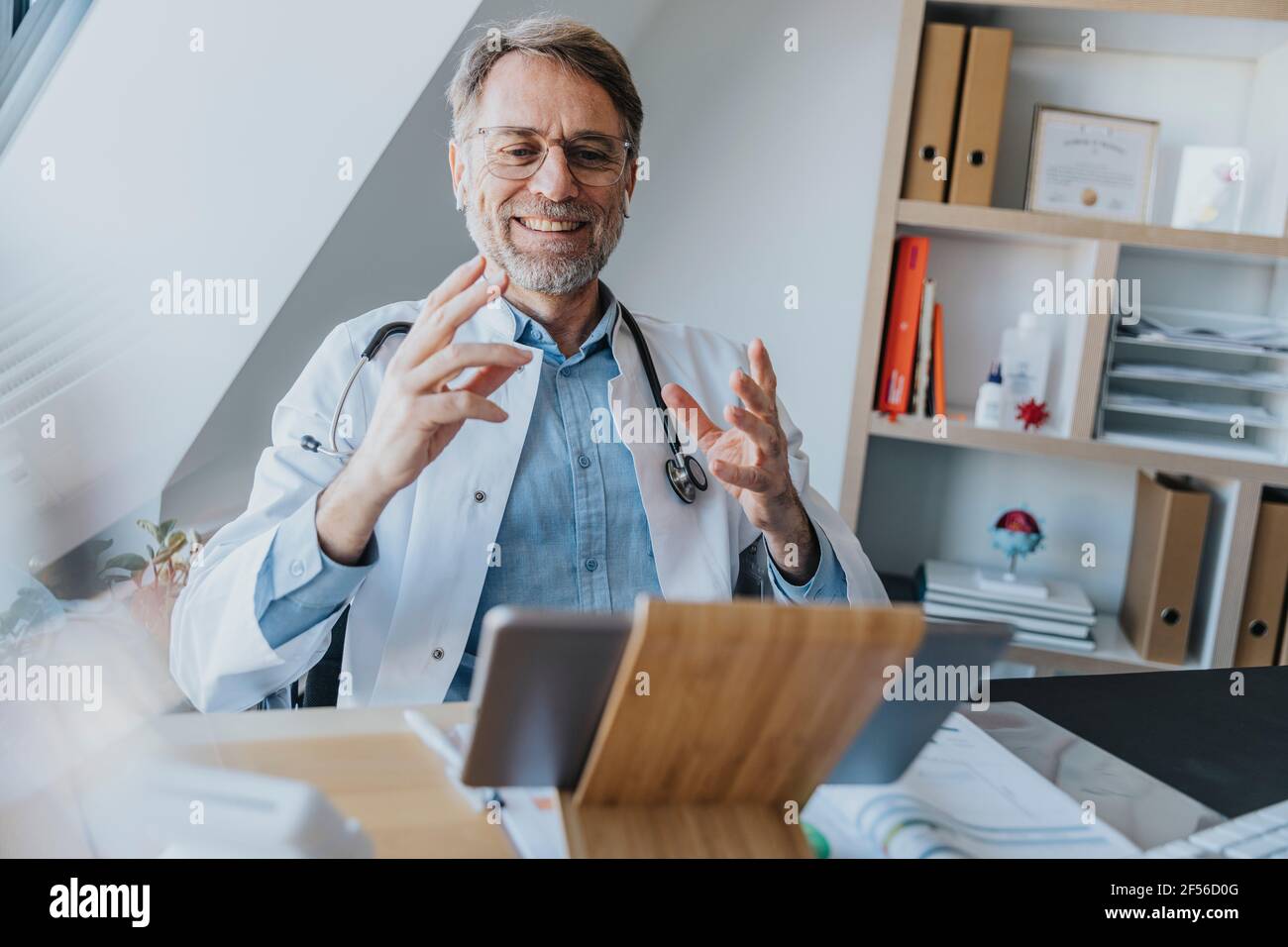 Male doctor gesturing while talking on video call over digital tablet ...