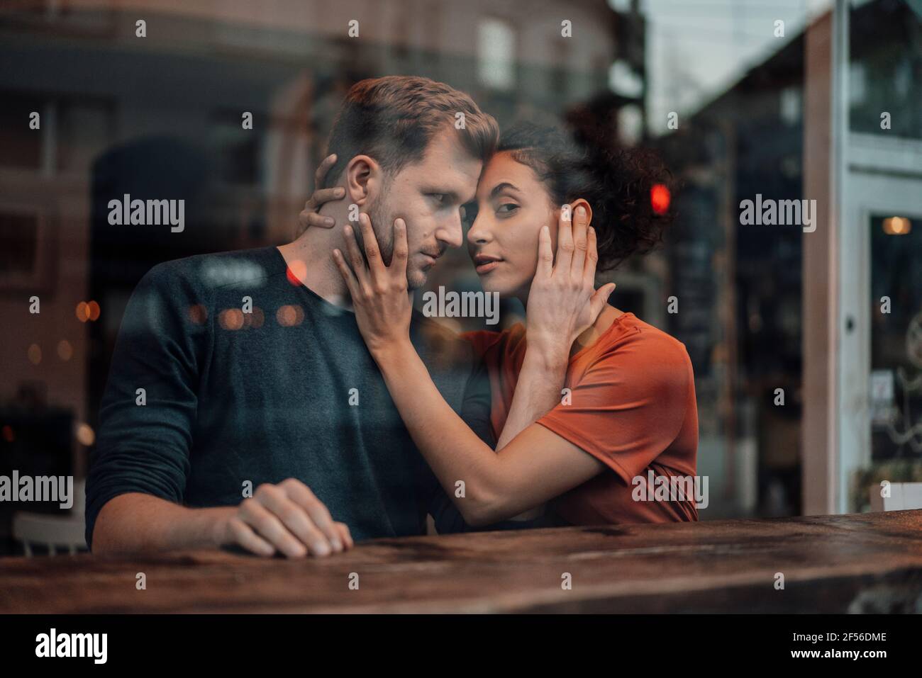Romantic couple touching each others faces at cafe seen through window ...