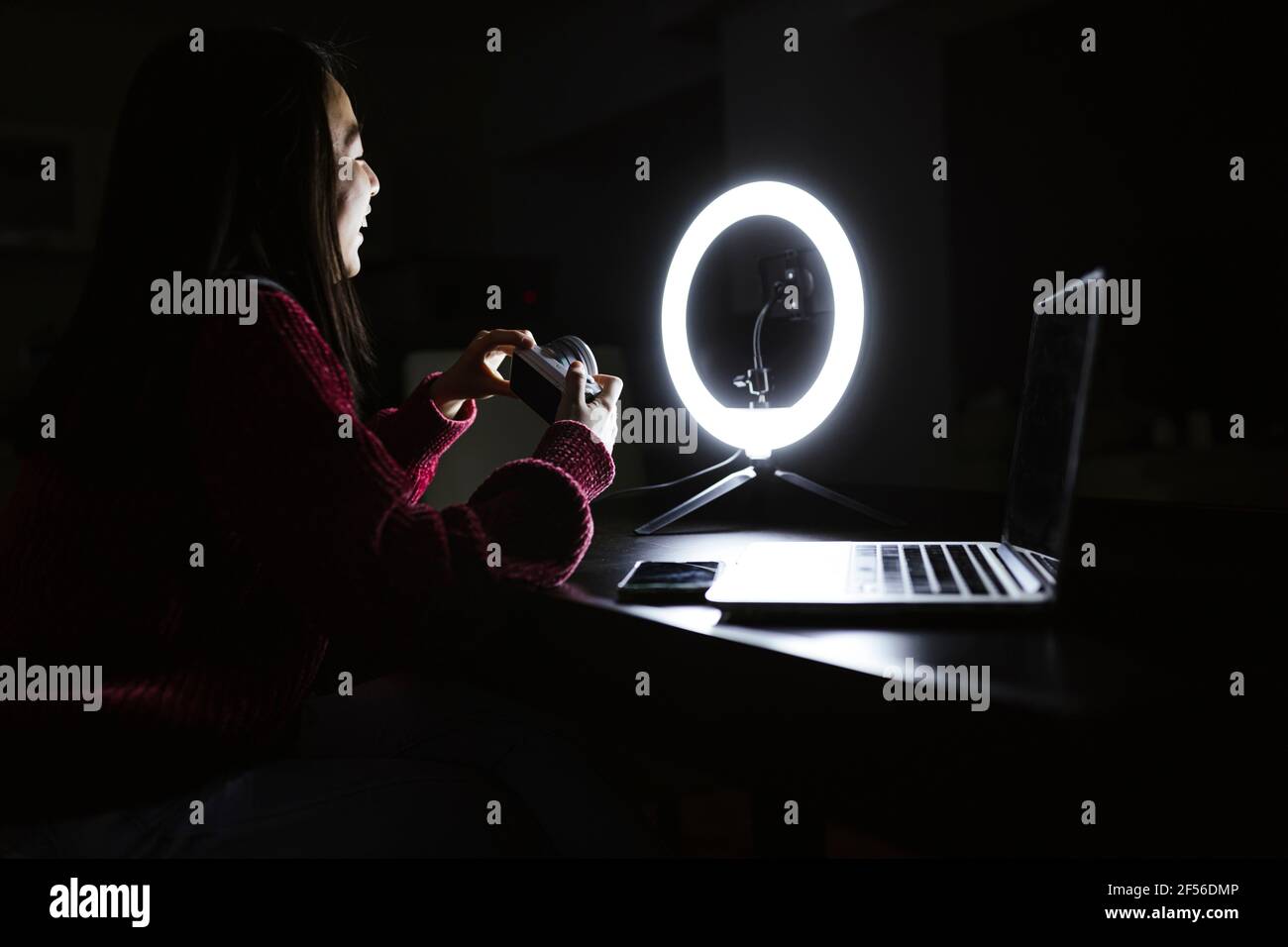 Cheerful female vlogger holding new camera in front of illuminated ring ...