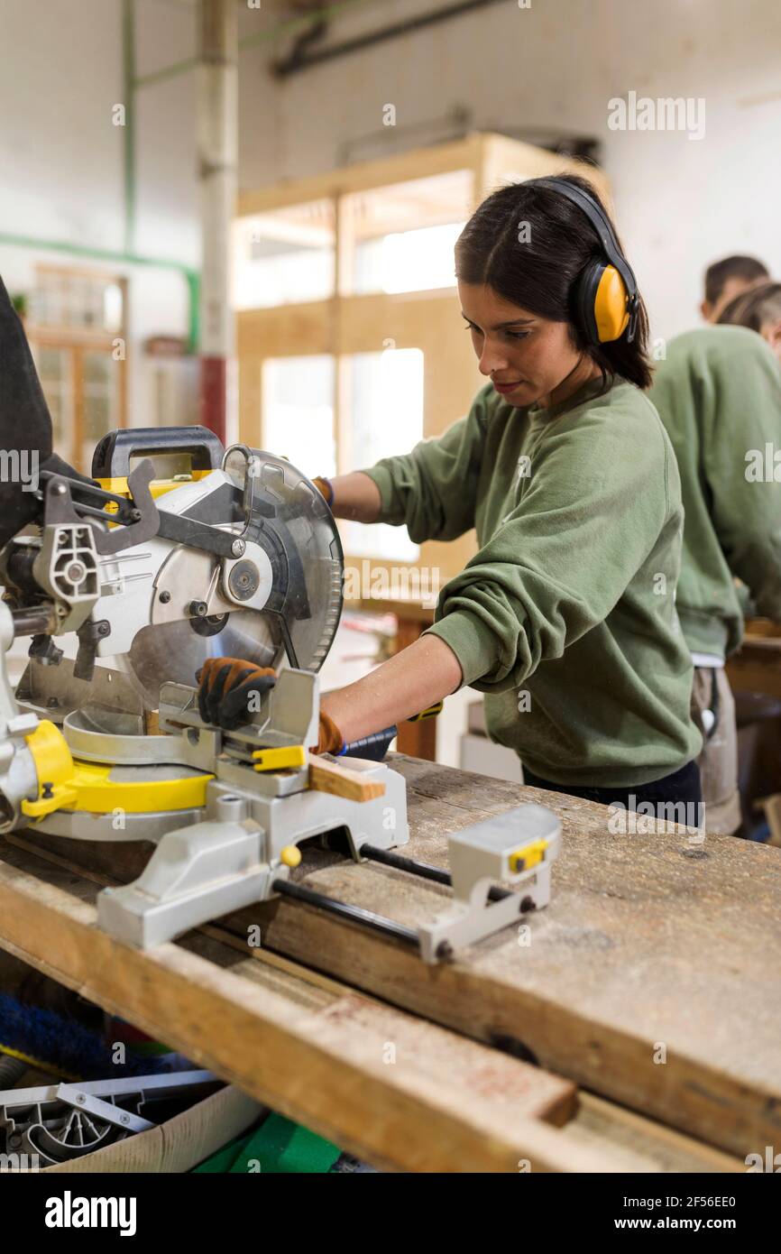 Female carpenter with ear muff using woodworking equipment at workbench ...