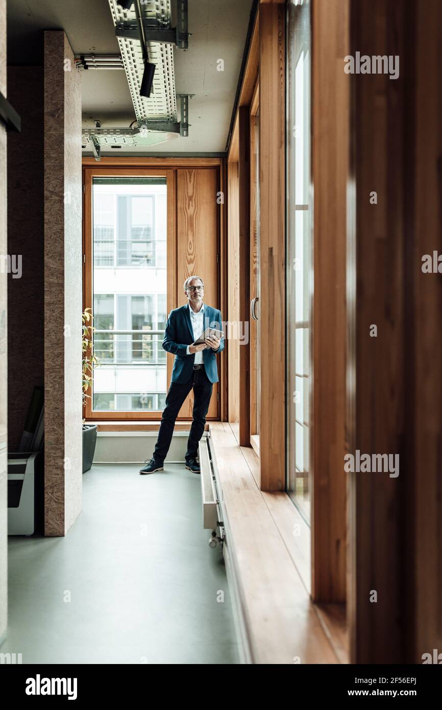 Businessman standing against window in office corridor Stock Photo - Alamy