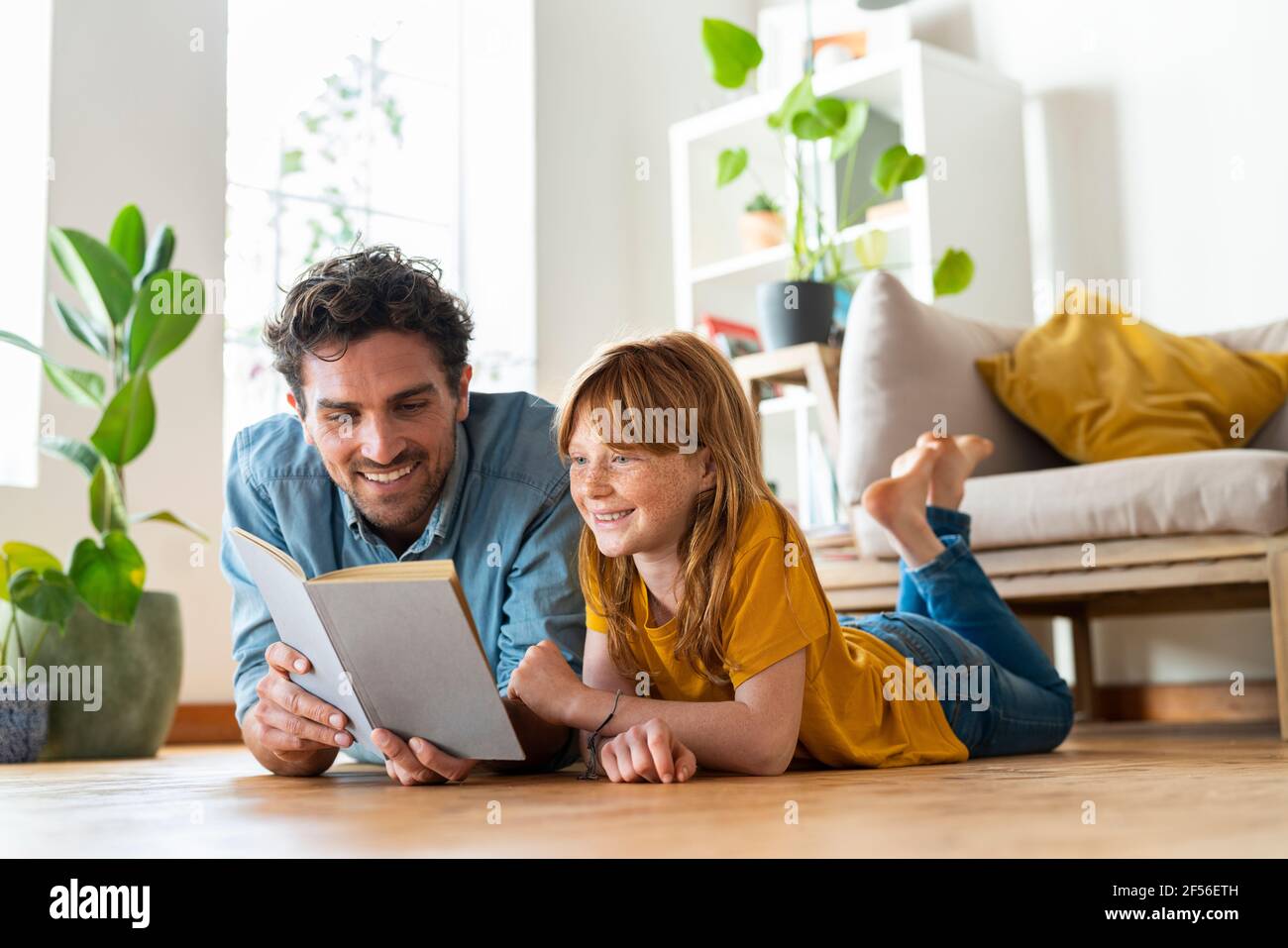 Smiling father and daughter reading book together while lying down on ...