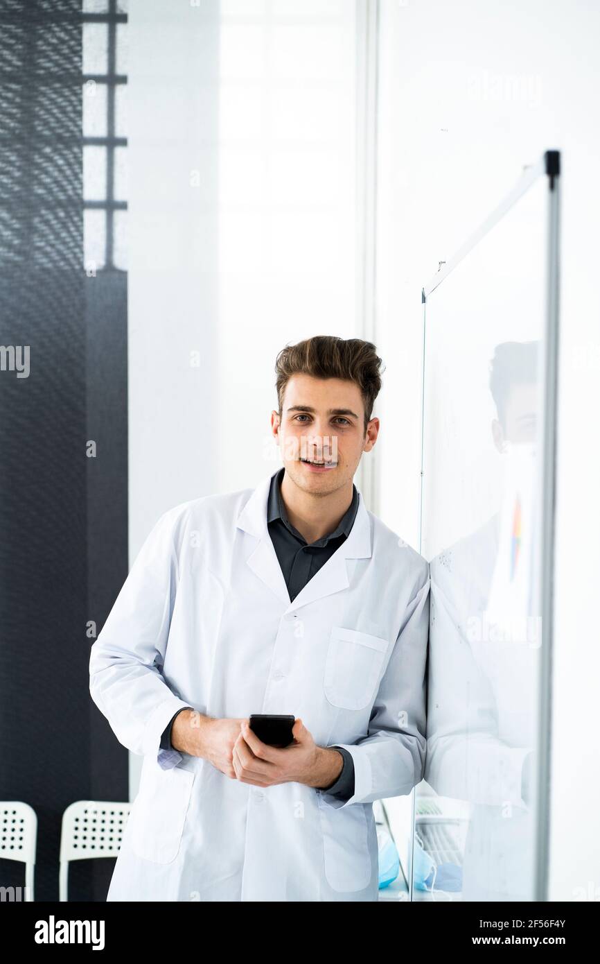 Male scientist with mobile phone leaning on whiteboard in laboratory ...