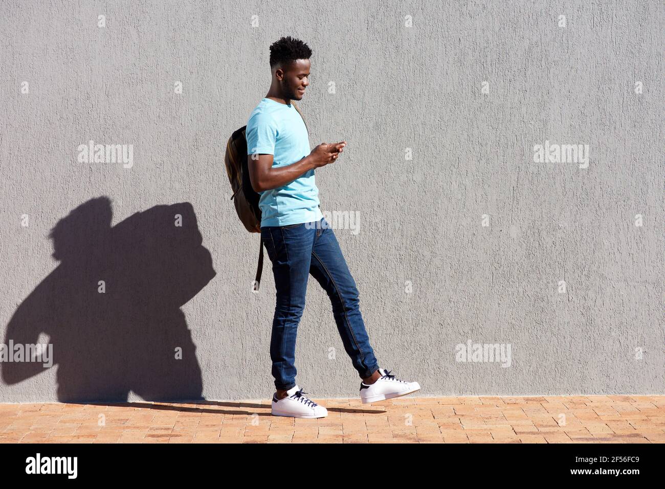 Full length portrait of college student walking with bag and mobile ...