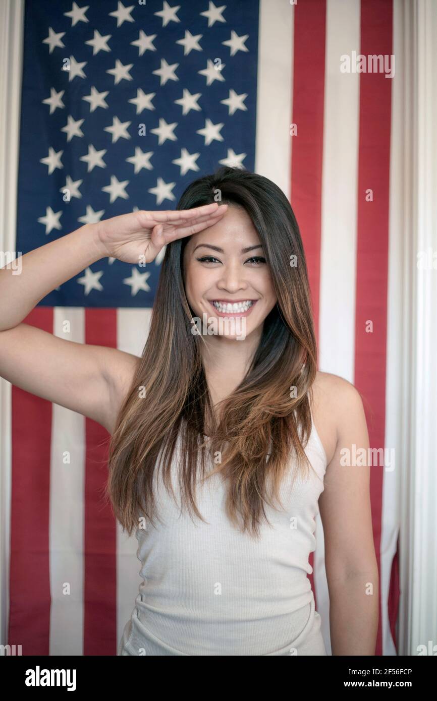 Beautiful woman saluting against American flag Stock Photo - Alamy