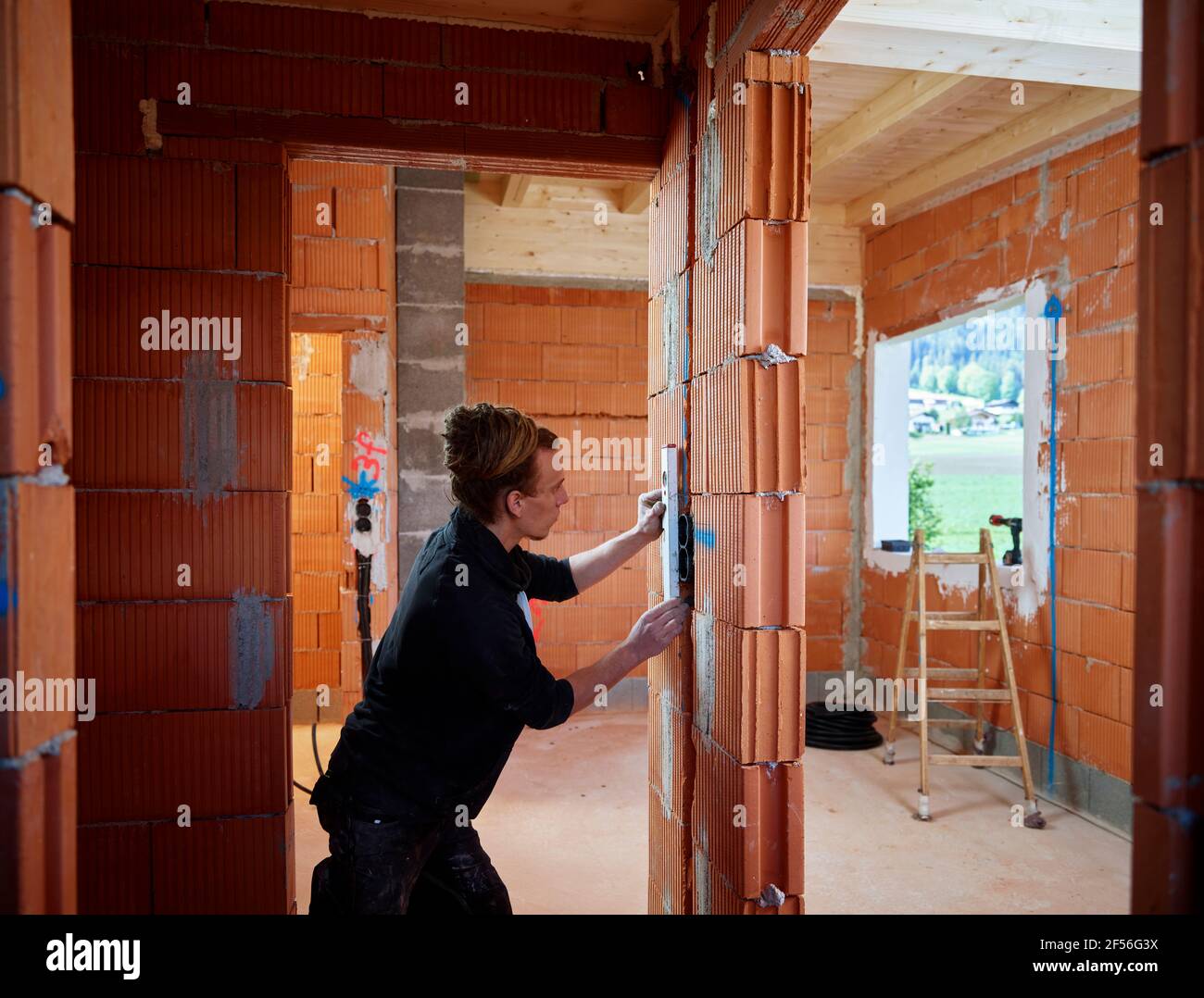 Concentrated male electrician using level instrument on brick wall at ...