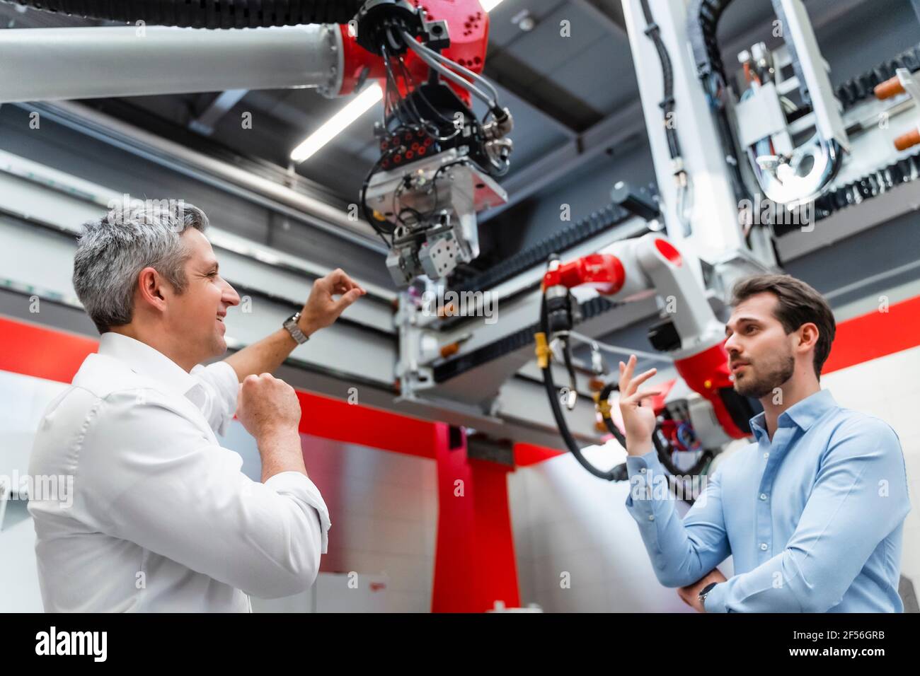 Smiling automation engineers discussing over robot arm in factory Stock ...