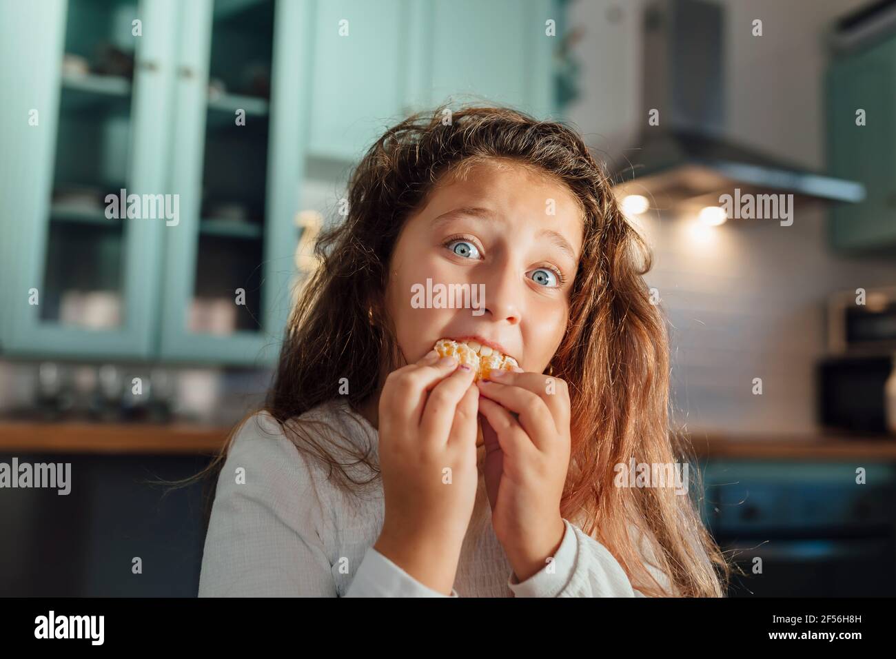 Girl with brown hair eating tangerine while sitting at dining table in ...