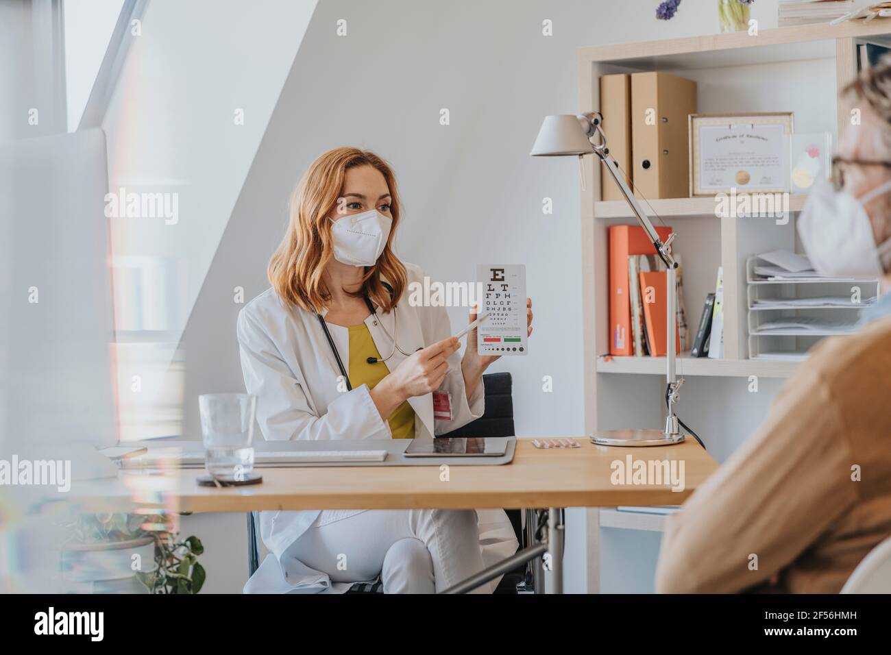 Ophthalmologist showing eye chart to patient while sitting at distant ...