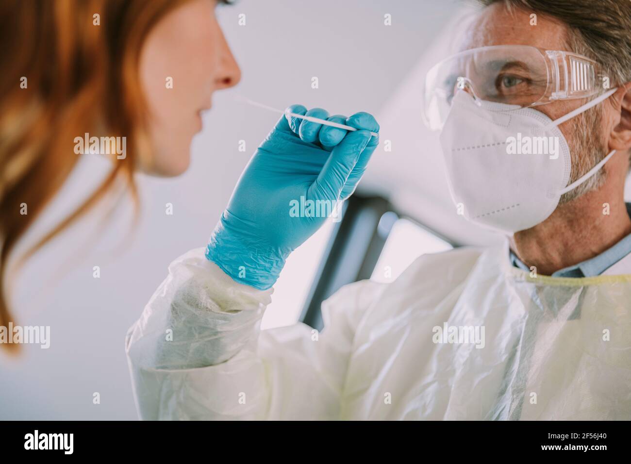 Male doctor wearing protective suit and face mask taking nasal swab ...
