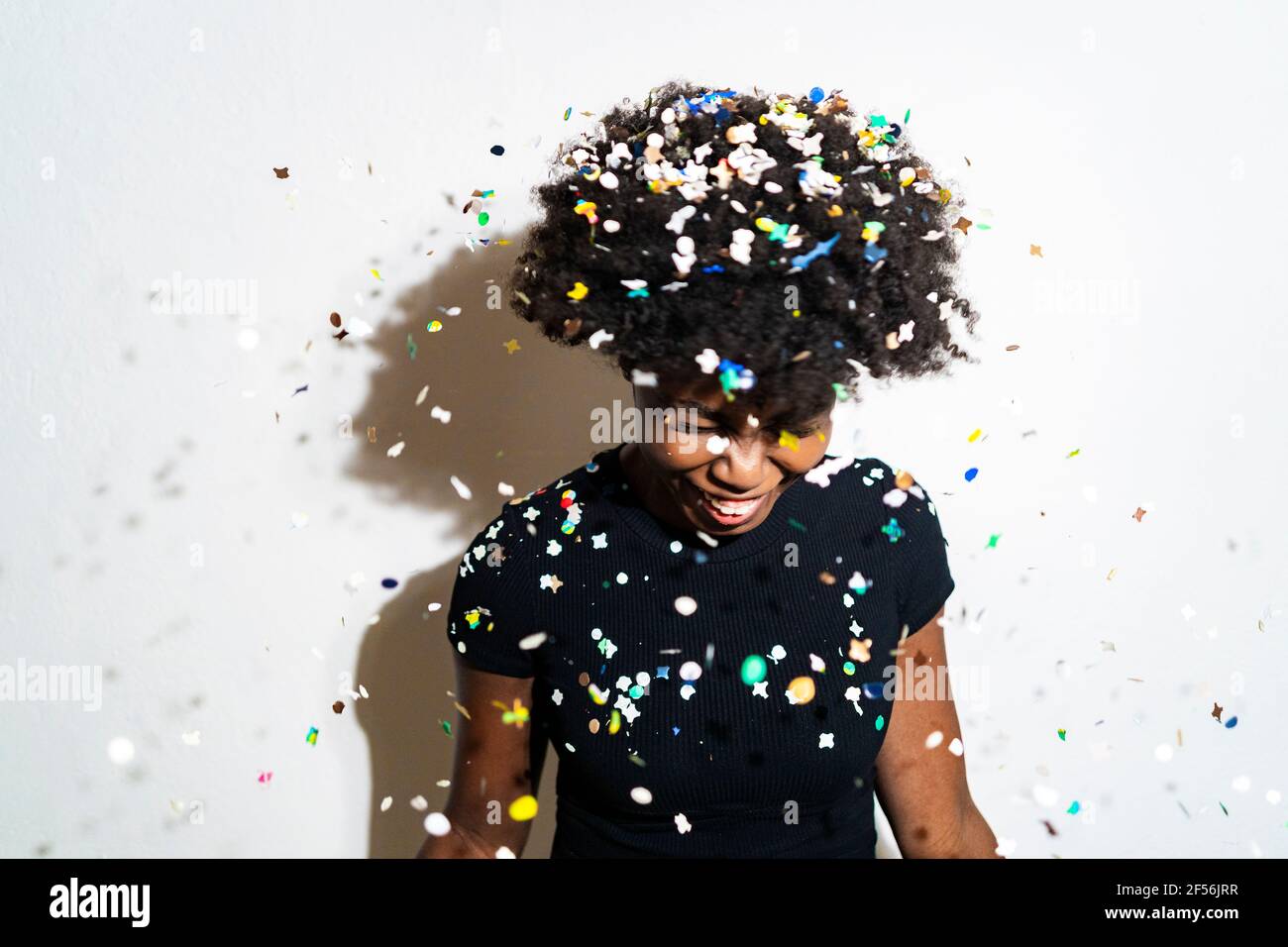 Smiling woman with confetti falling on head standing against white ...