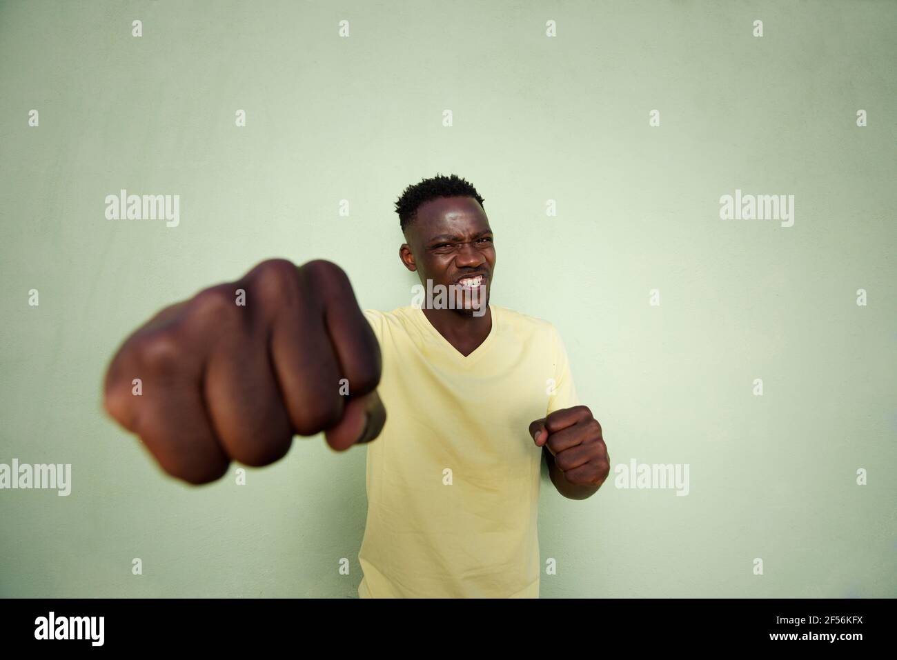 Wide angle portrait of aggressive young african man punching with fist ...