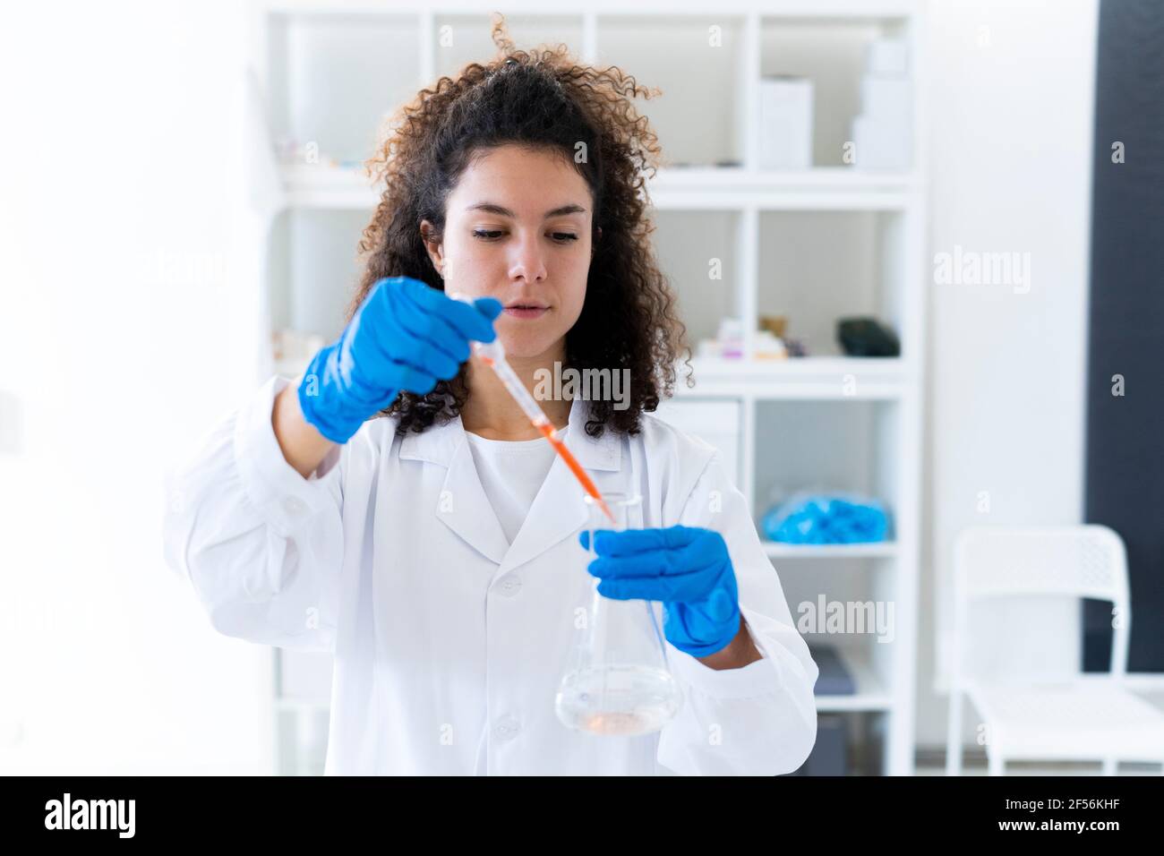 Young female scientist experimenting with chemical solution in beaker ...