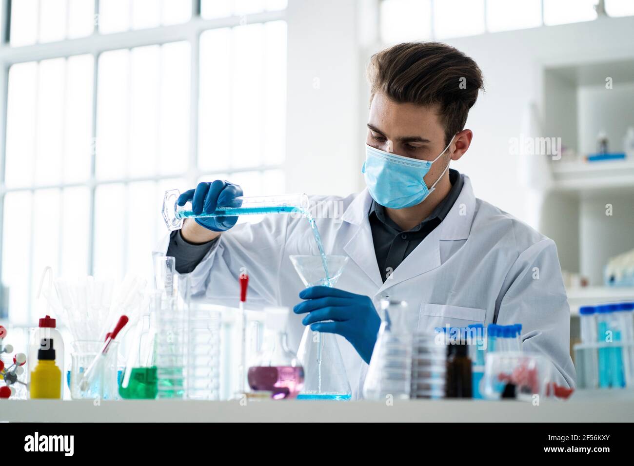 Male scientist pouring liquid in flask at laboratory during pandemic ...