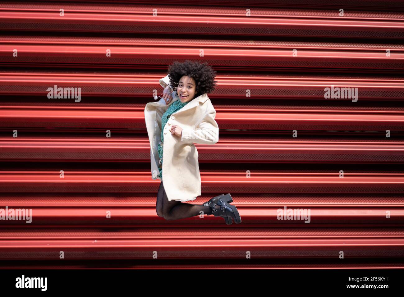 Happy afro woman jumping against red shutter Stock Photo - Alamy