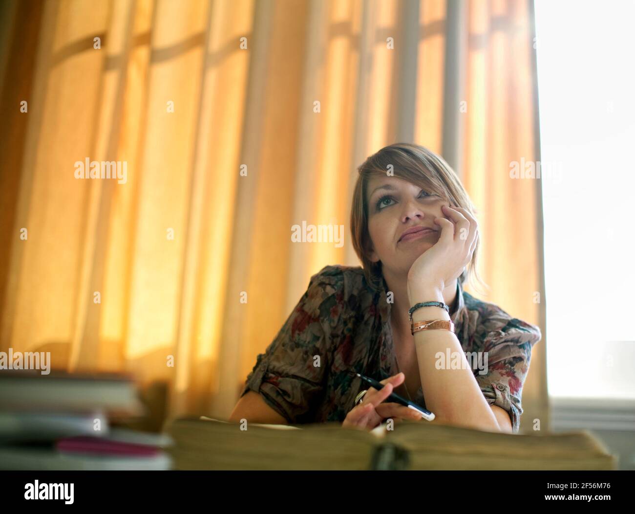 Contemplating young woman with books in library Stock Photo - Alamy