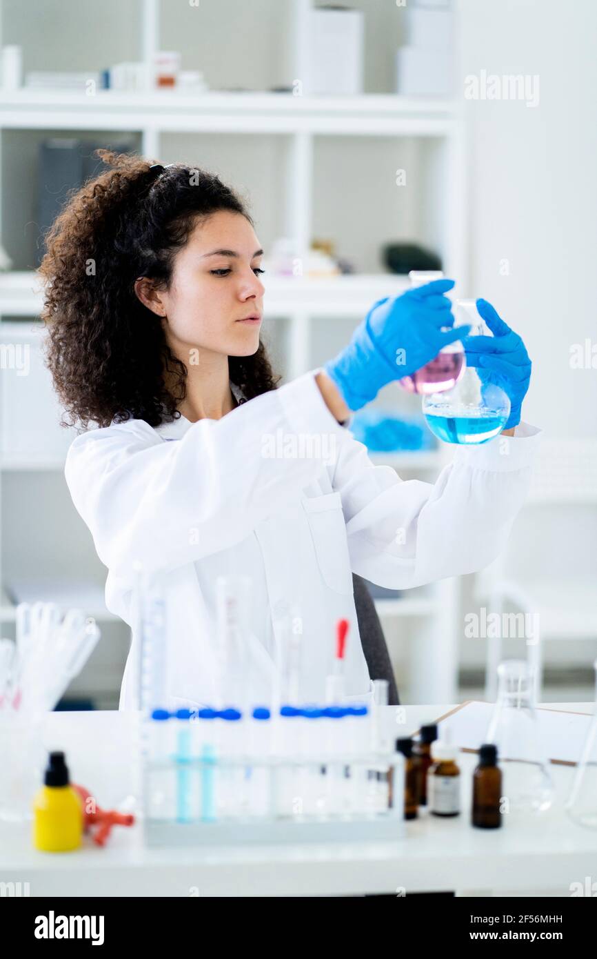 Young female researcher testing chemical solution in beaker at hospital ...