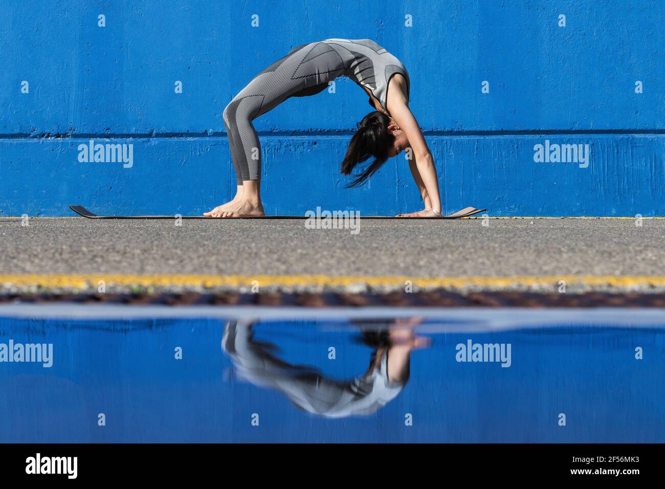 Woman doing back bend yoga pose by blue wall Stock Photo - Alamy