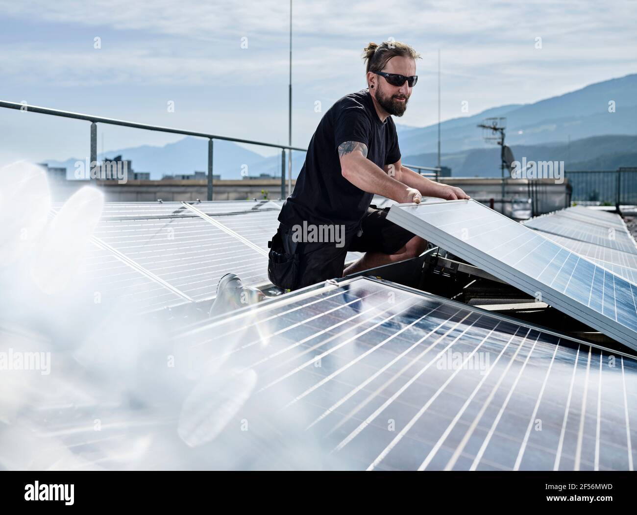 Male electrician installing solar panels on building terrace during ...