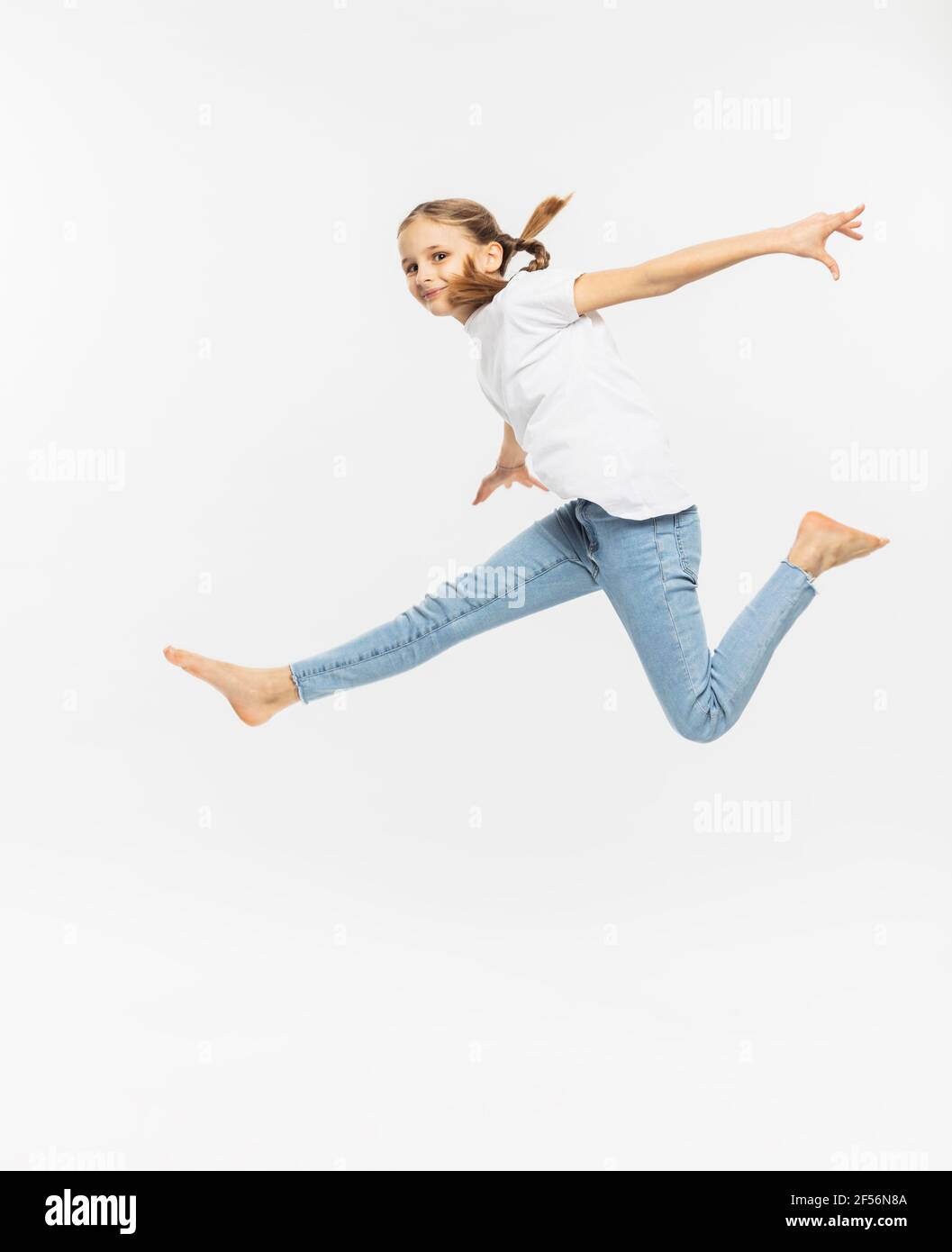 Girl with arms outstretched gesturing while jumping by white background ...