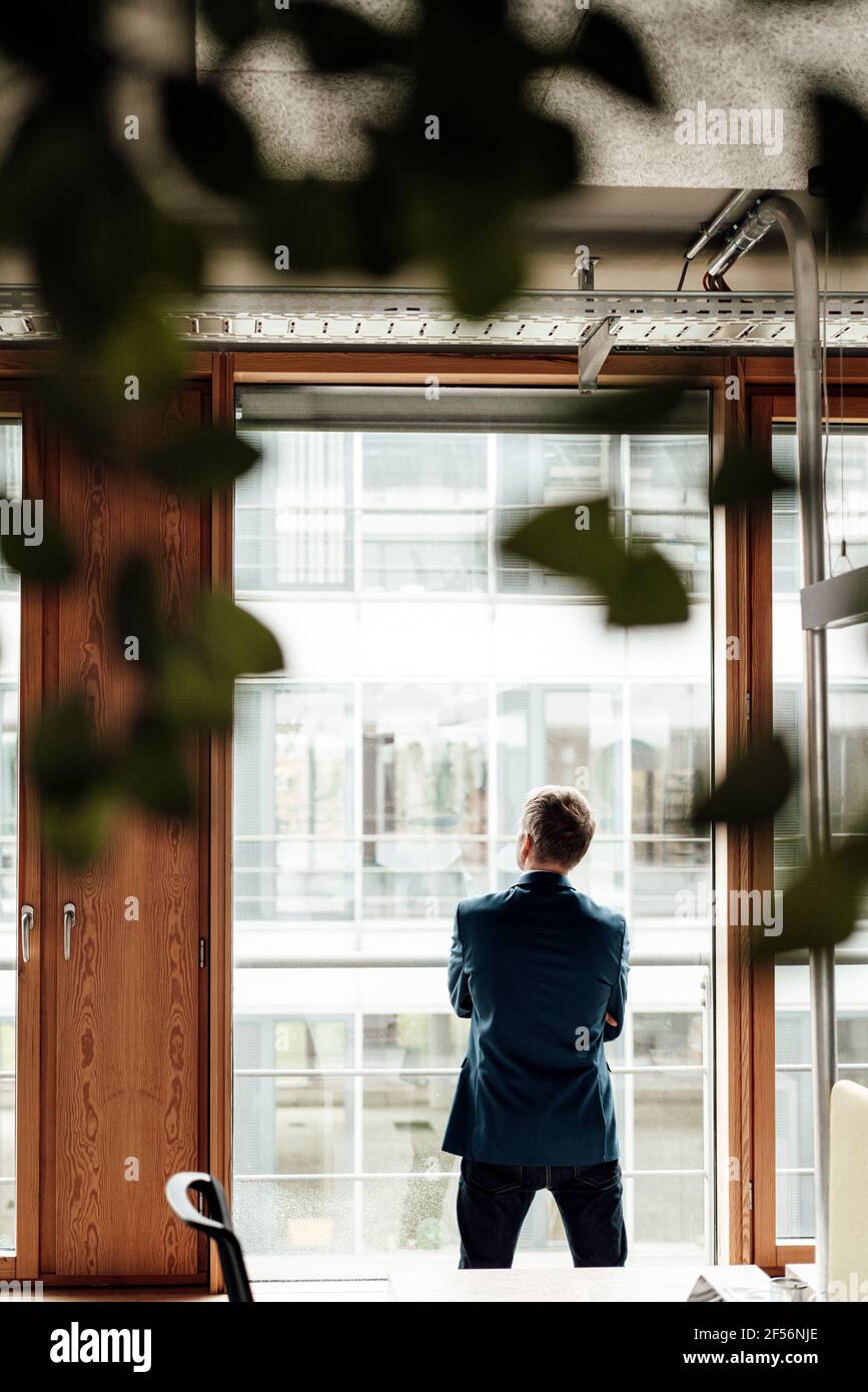 Male business professional looking through window in office Stock Photo ...