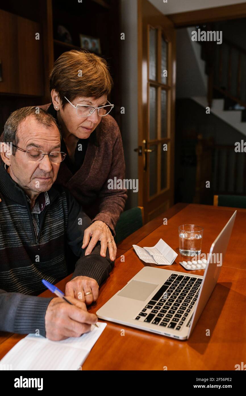 Senior man with social worker writing on book while using laptop at ...