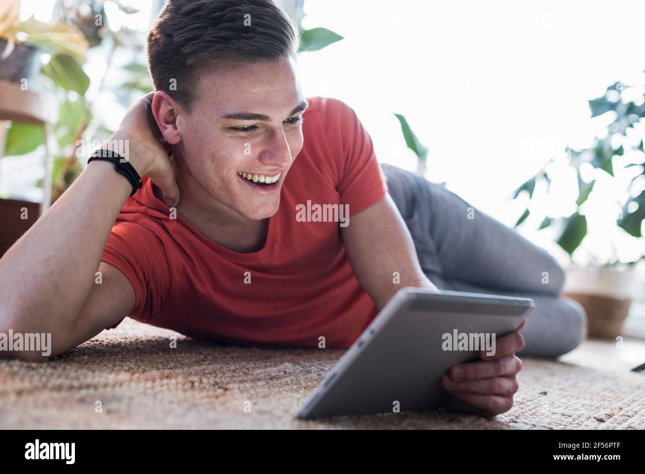 Happy young man watching video on digital tablet while lying on carpet ...