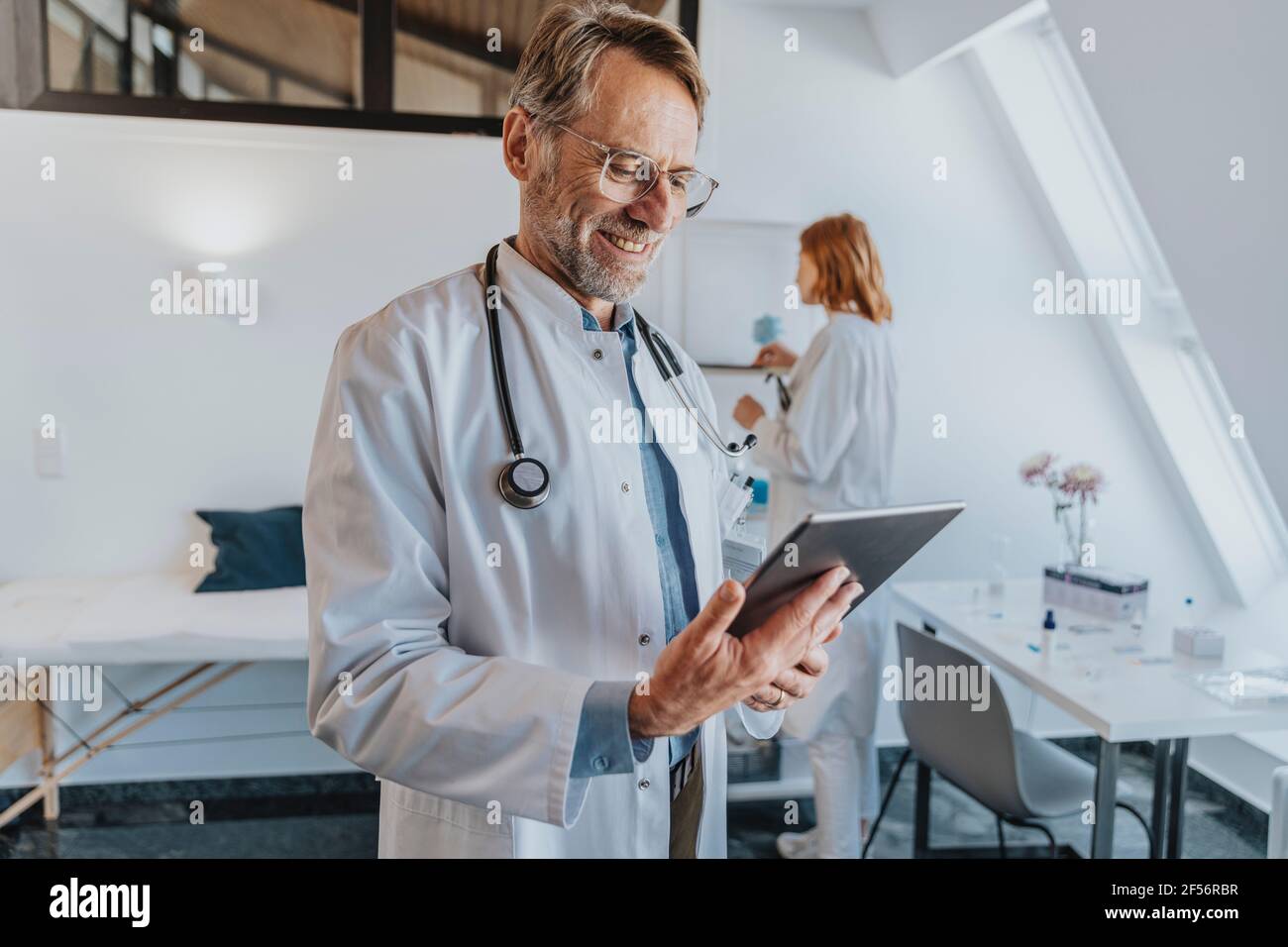 General practitioner using digital tablet while standing with coworker ...