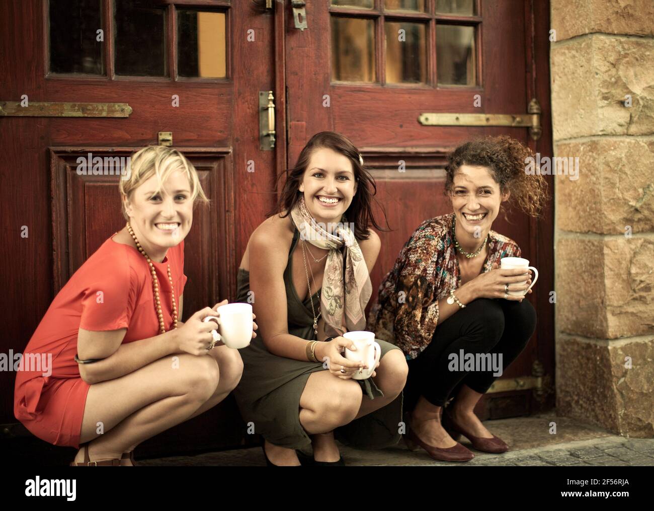 Young women with coffee cup smiling while crouching against door Stock ...