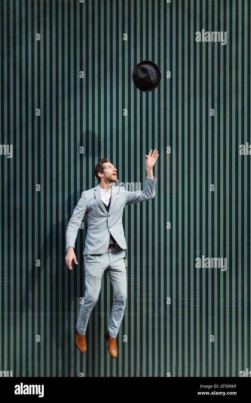Businessman jumping while throwing hat against wall Stock Photo - Alamy