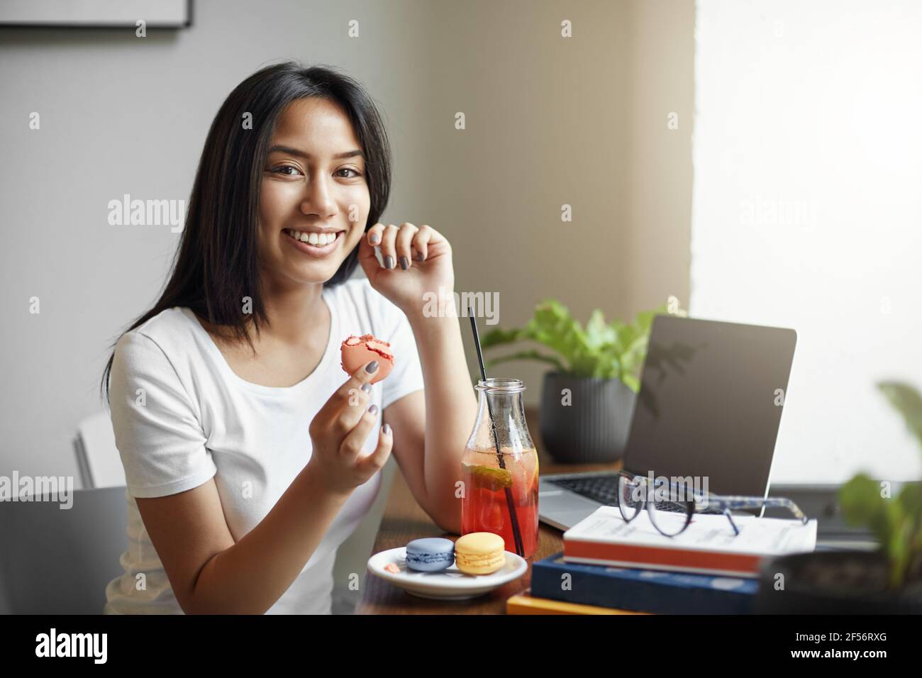 Female asian student eating macaron cake and drinking lemonade while ...