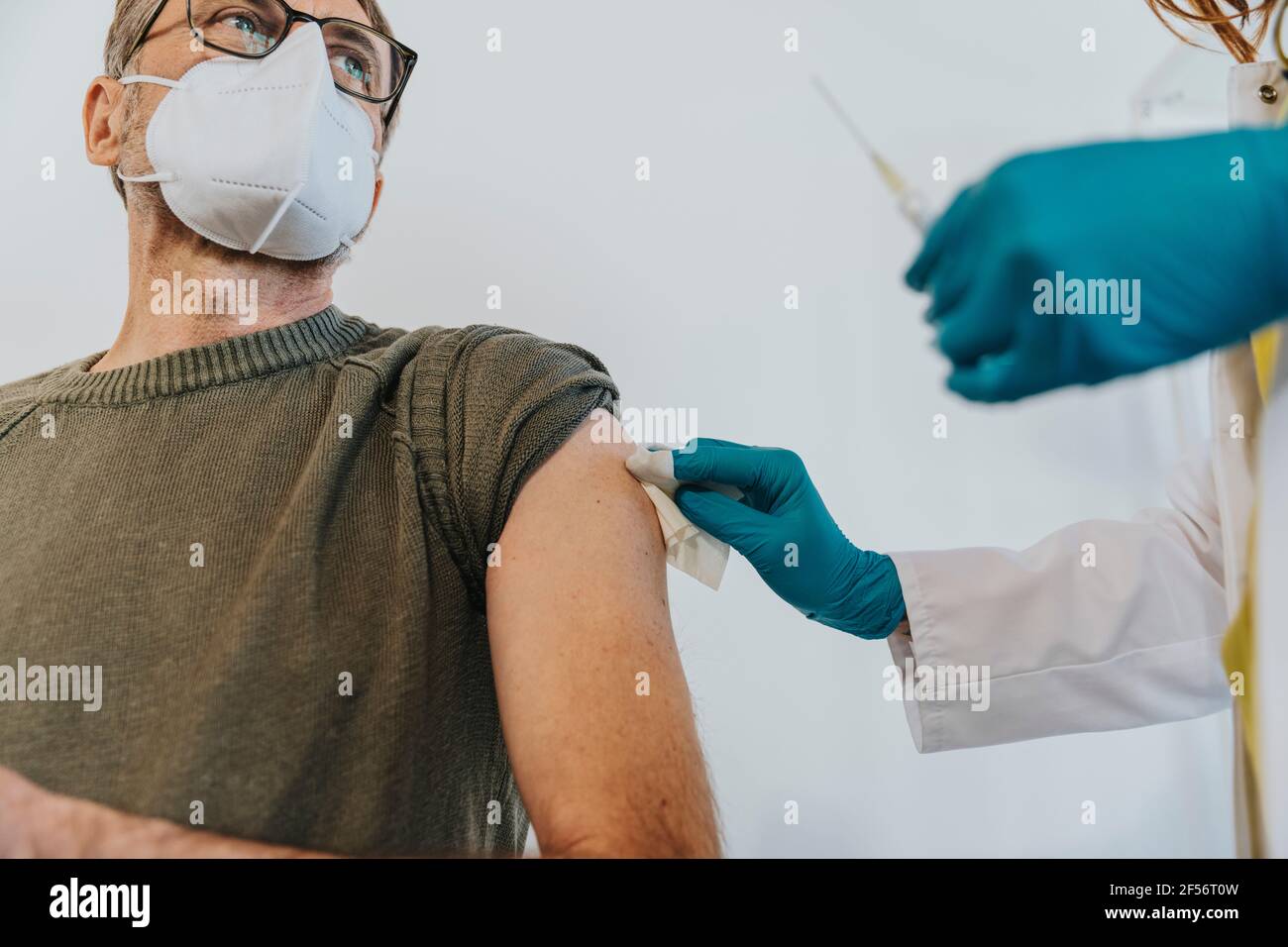 Doctor with syringe disinfecting patient arm while standing at ...