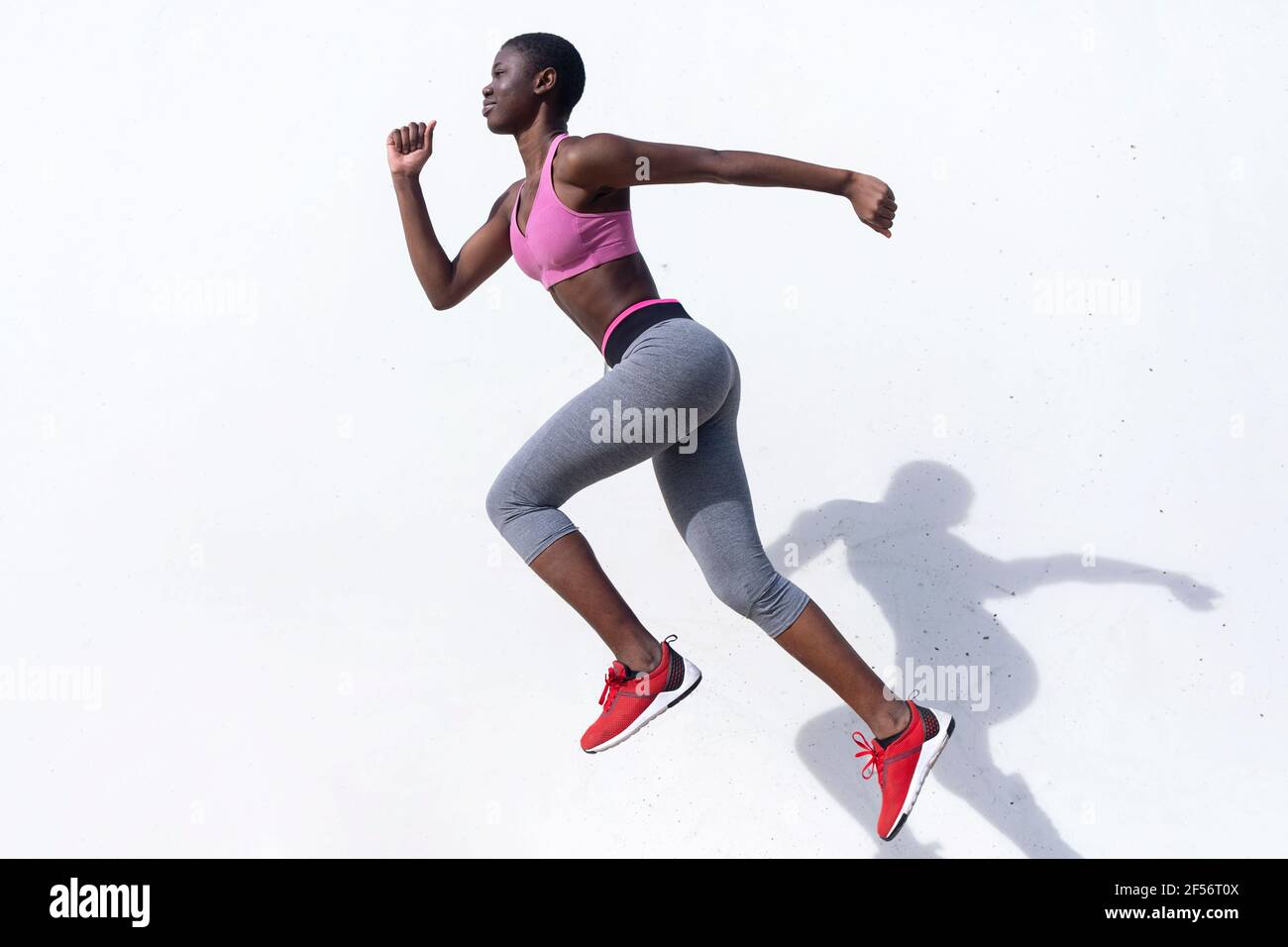 Female runner jumping while practicing against white wall Stock Photo ...