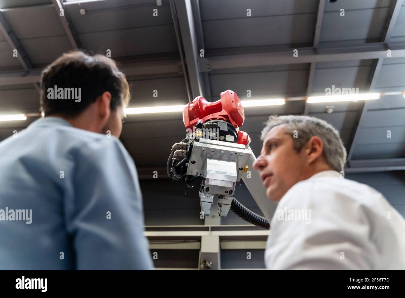 Male engineers discussing at robotic arm in factory Stock Photo - Alamy