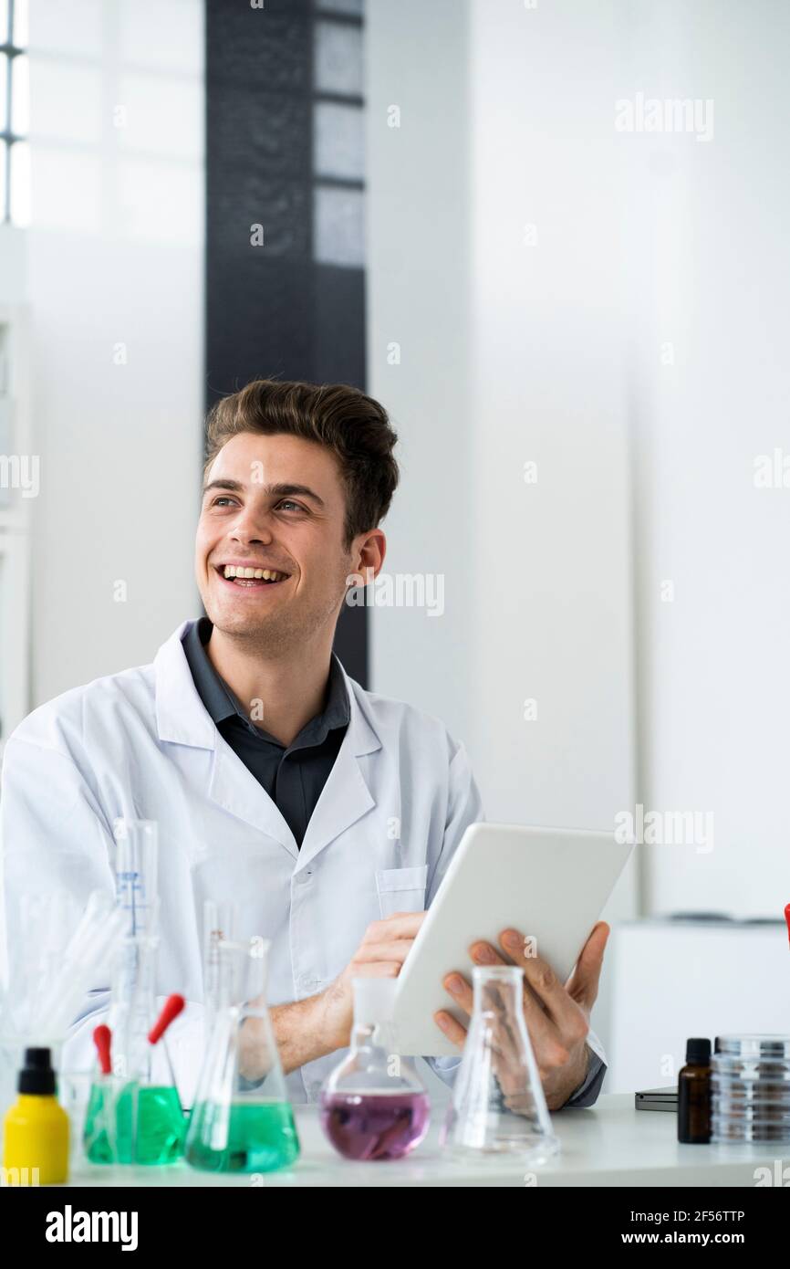 Laughing male scientist with digital tablet while looking away in ...