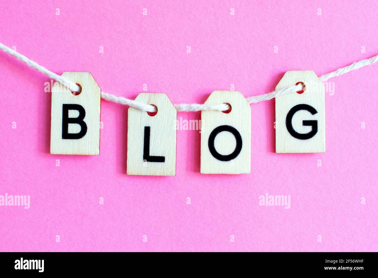 The word BLOG spelt with letter tiles hanging over a pink background ...