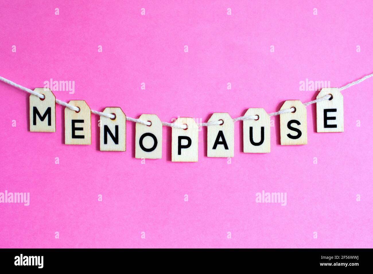 The word MENOPAUSE spelt with letter tiles hanging over a pink ...
