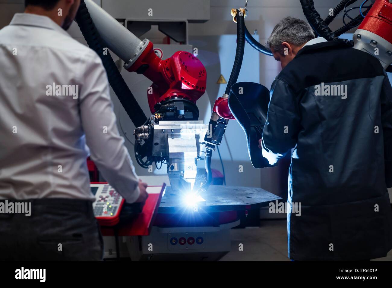 Male welder examining robotics while standing by young engineer working ...