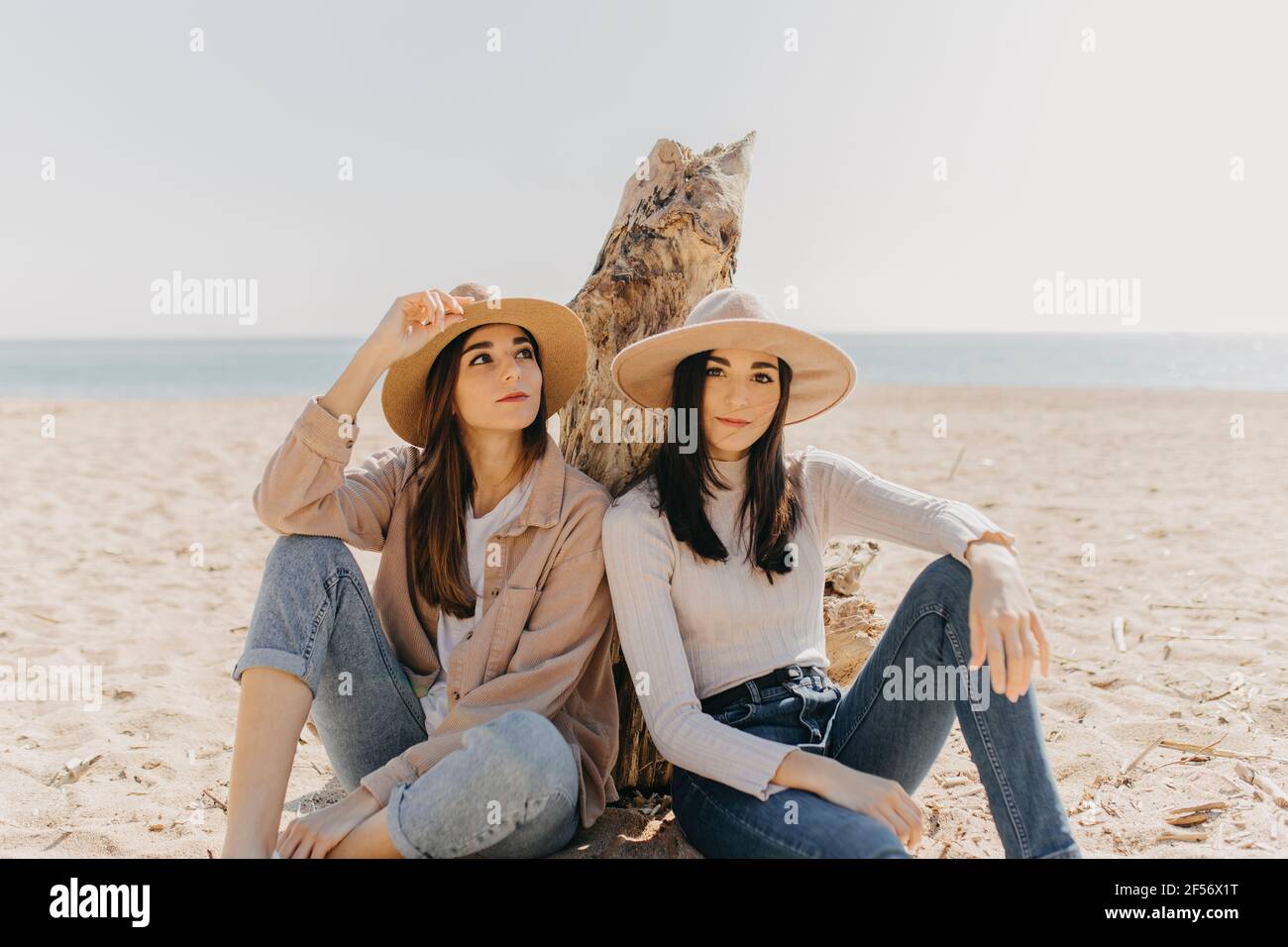 Female twins sitting side by side at beach on sunny day Stock Photo - Alamy