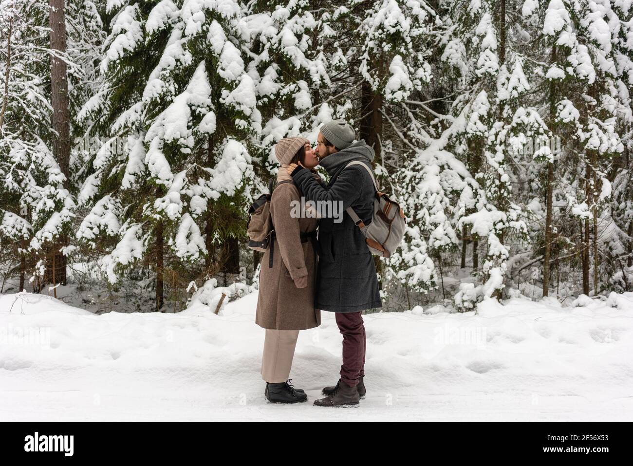 Young couple with backpack kissing while standing in forest Stock Photo ...