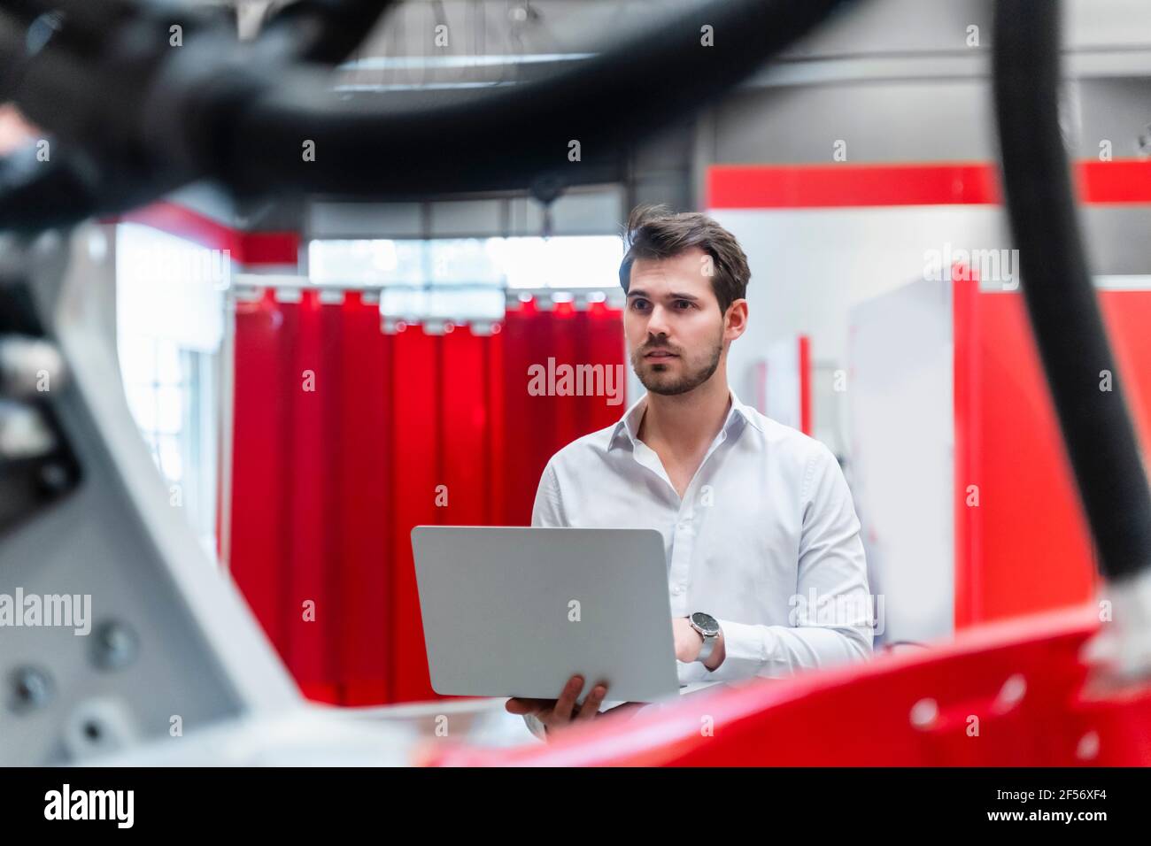 Male engineer with laptop seen through robotics in factory Stock Photo ...