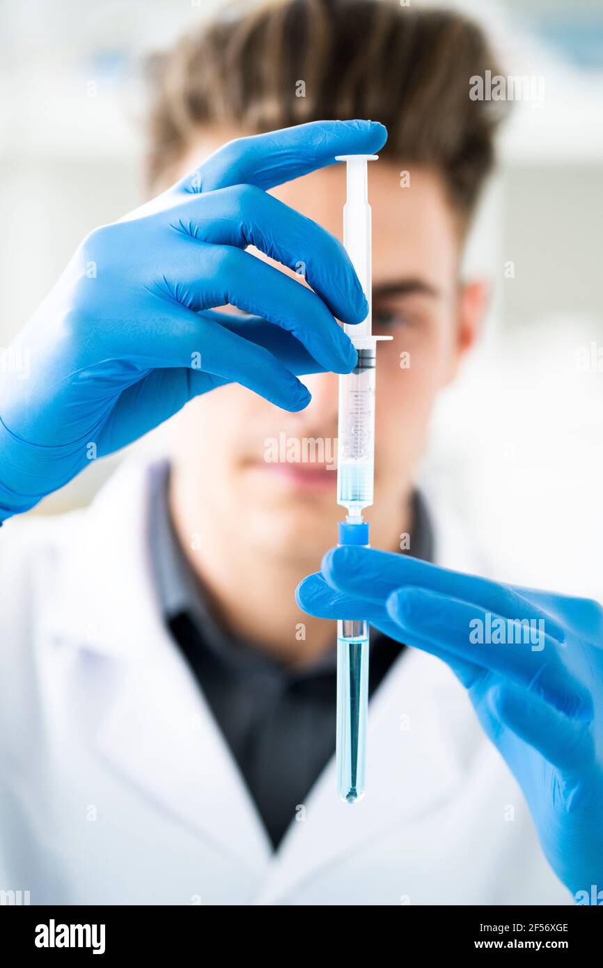 Male scientist mixing liquid in test tube through syringe in laboratory ...
