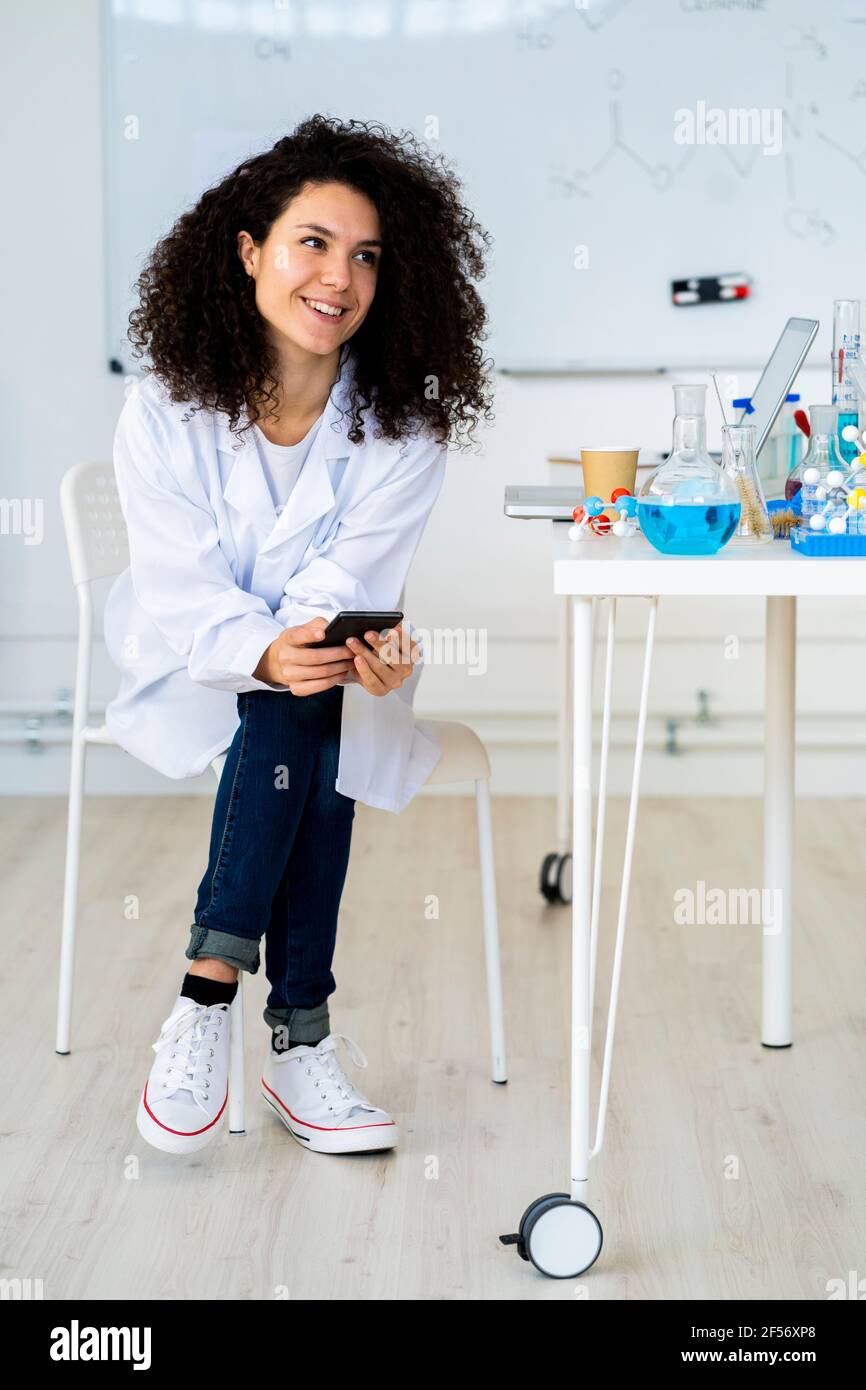 Smiling female researcher with mobile phone looking away at laboratory ...