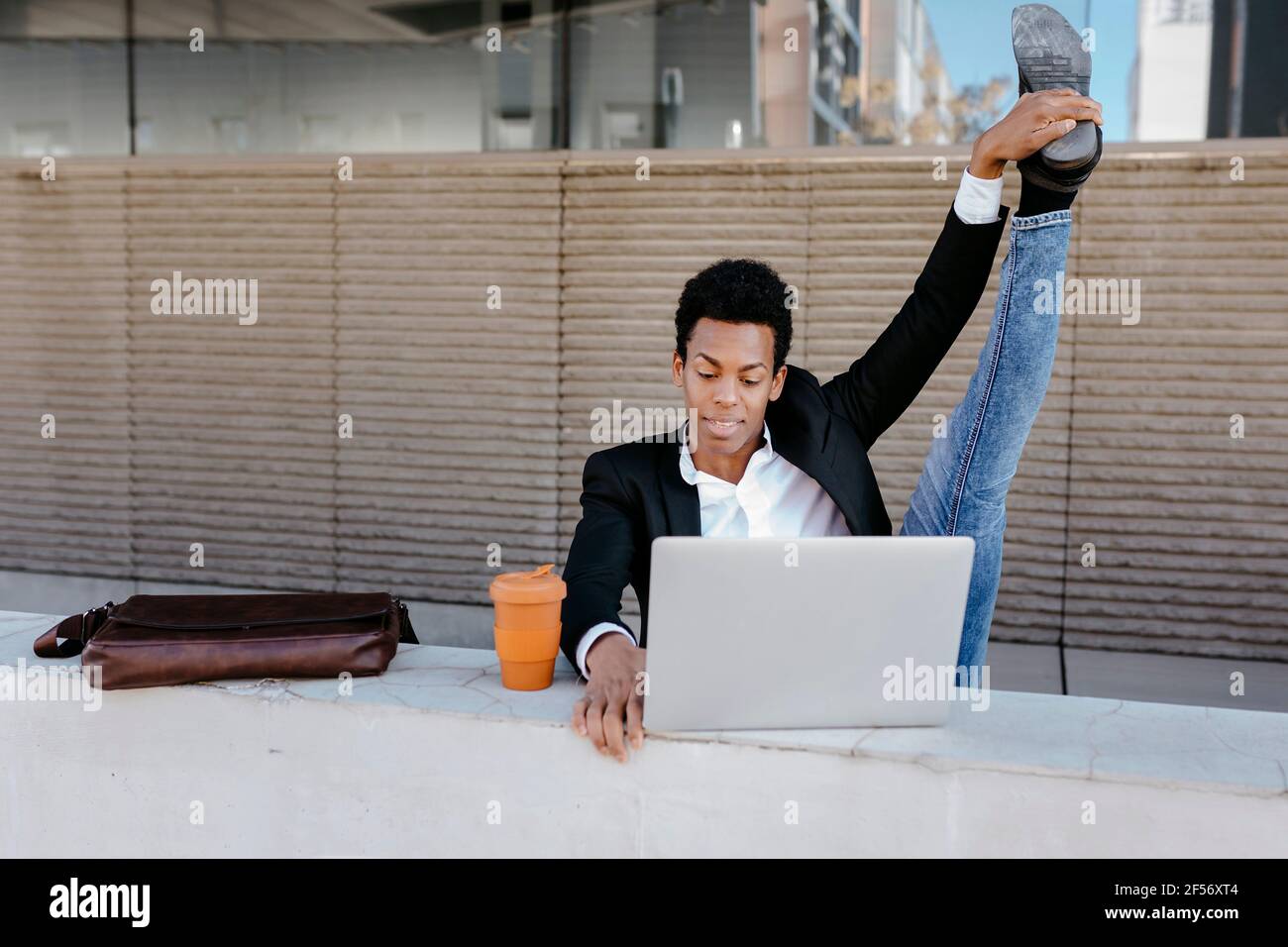 Flexible male entrepreneur using laptop while sitting at retaining wall ...